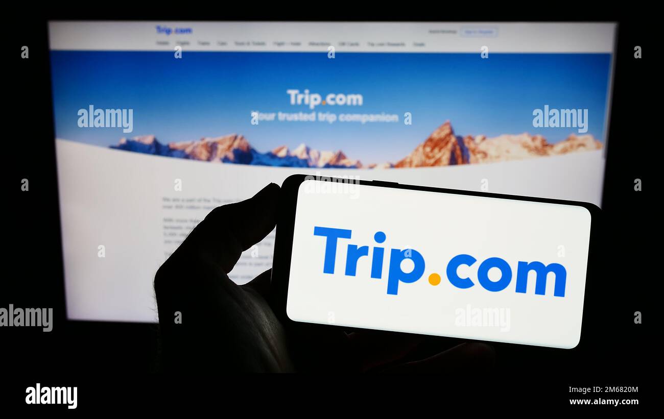 Personne tenant un smartphone avec le logo de la compagnie de voyage chinoise Trip.com Group ...