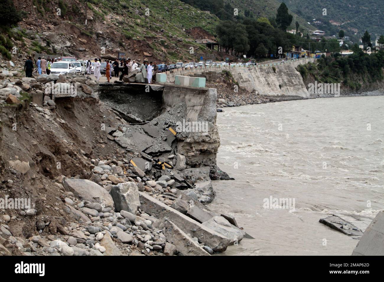 Passengers wait by a damaged road next to floodwaters, in Bahrain ...