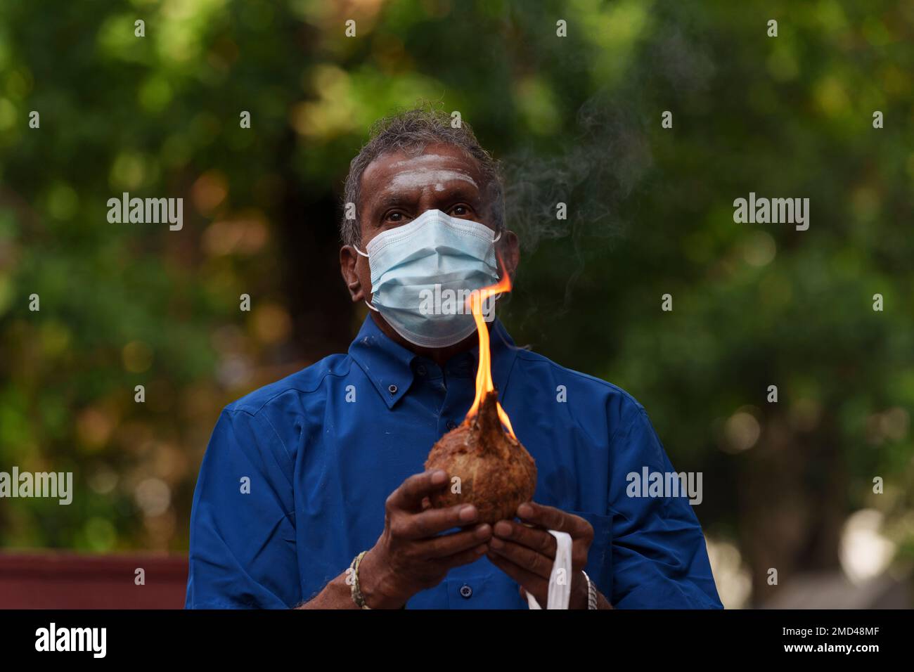 A Indian man prays with lit coconut as an offering outside a temple ...