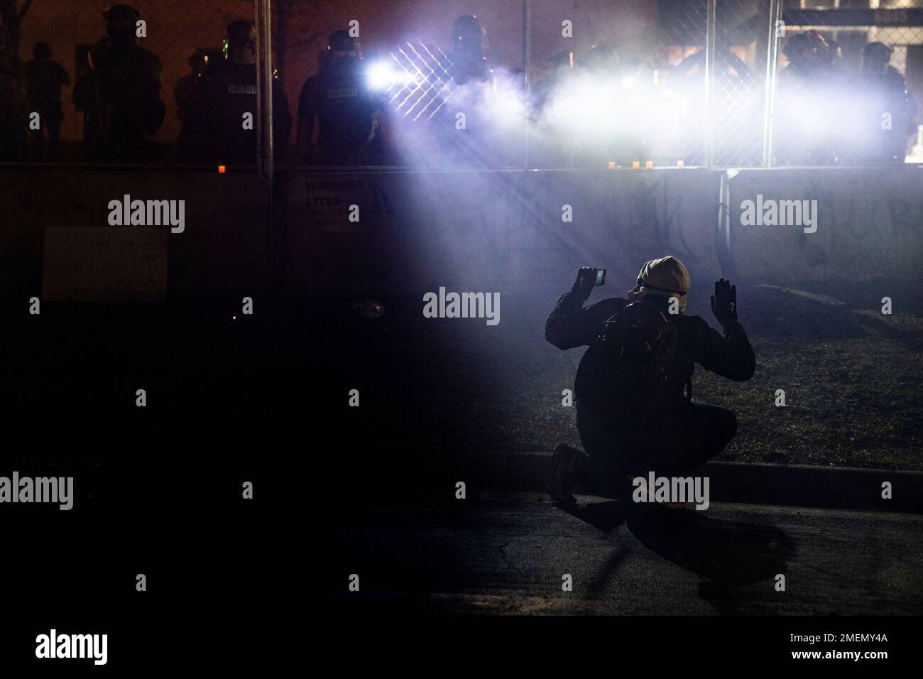 Police shine lights on a demonstrator with raised hands during a ...