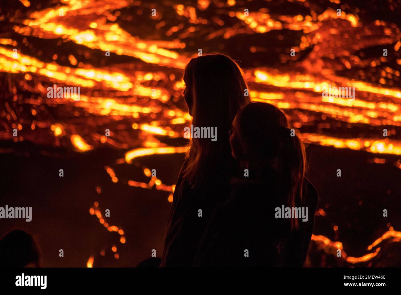 People watch as lava flows from an eruption of a volcano on the ...