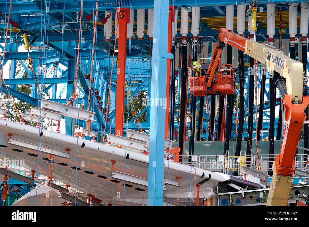 A worker suspended in an overhead basket look down at the wing on a ...