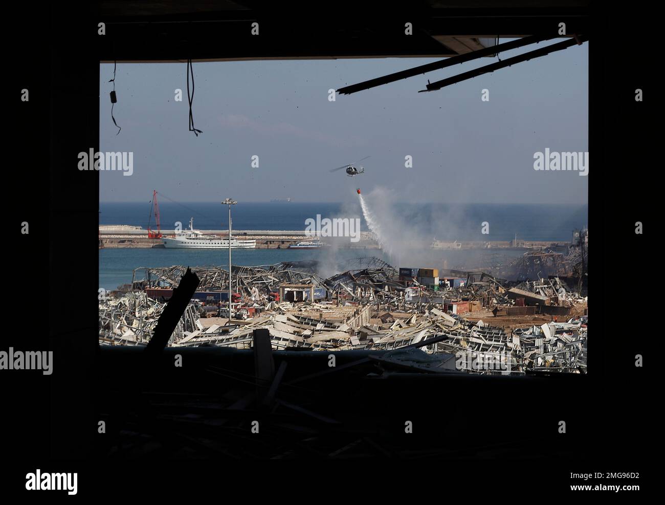 A Lebanese army helicopter seen through a damaged apartment drops water ...