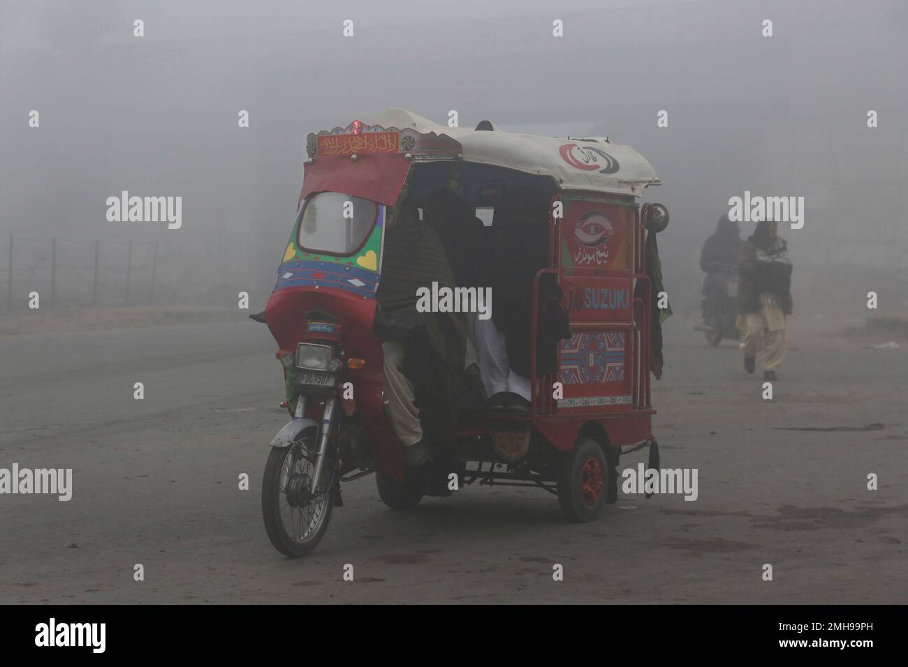 People travel in an auto rickshaw as smog envelops a road in Lahore ...