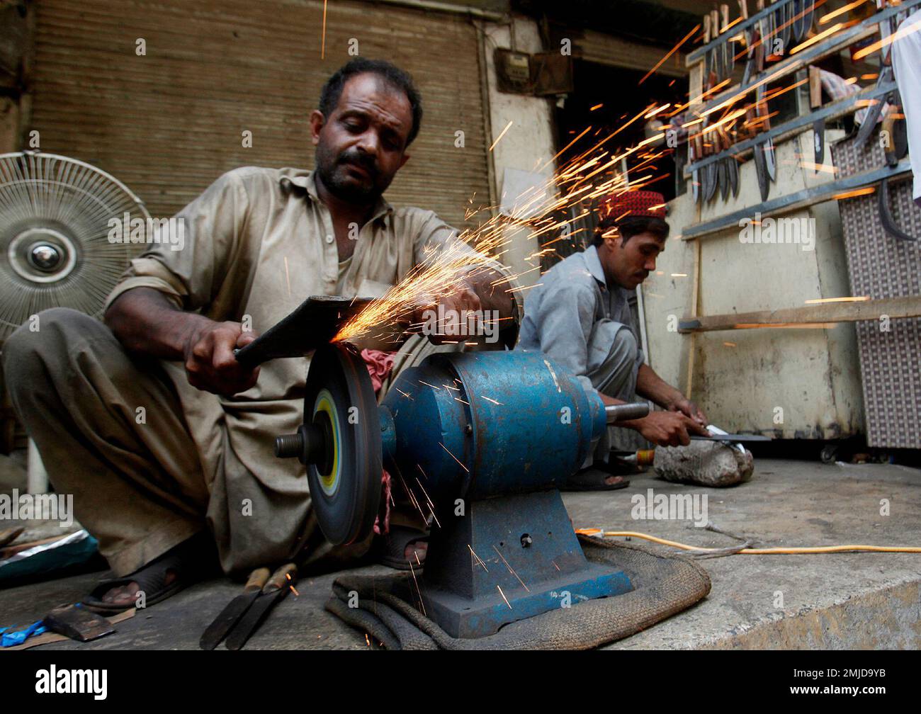 A Pakistani vendor sharpen axe for a customer, which will use to animal ...