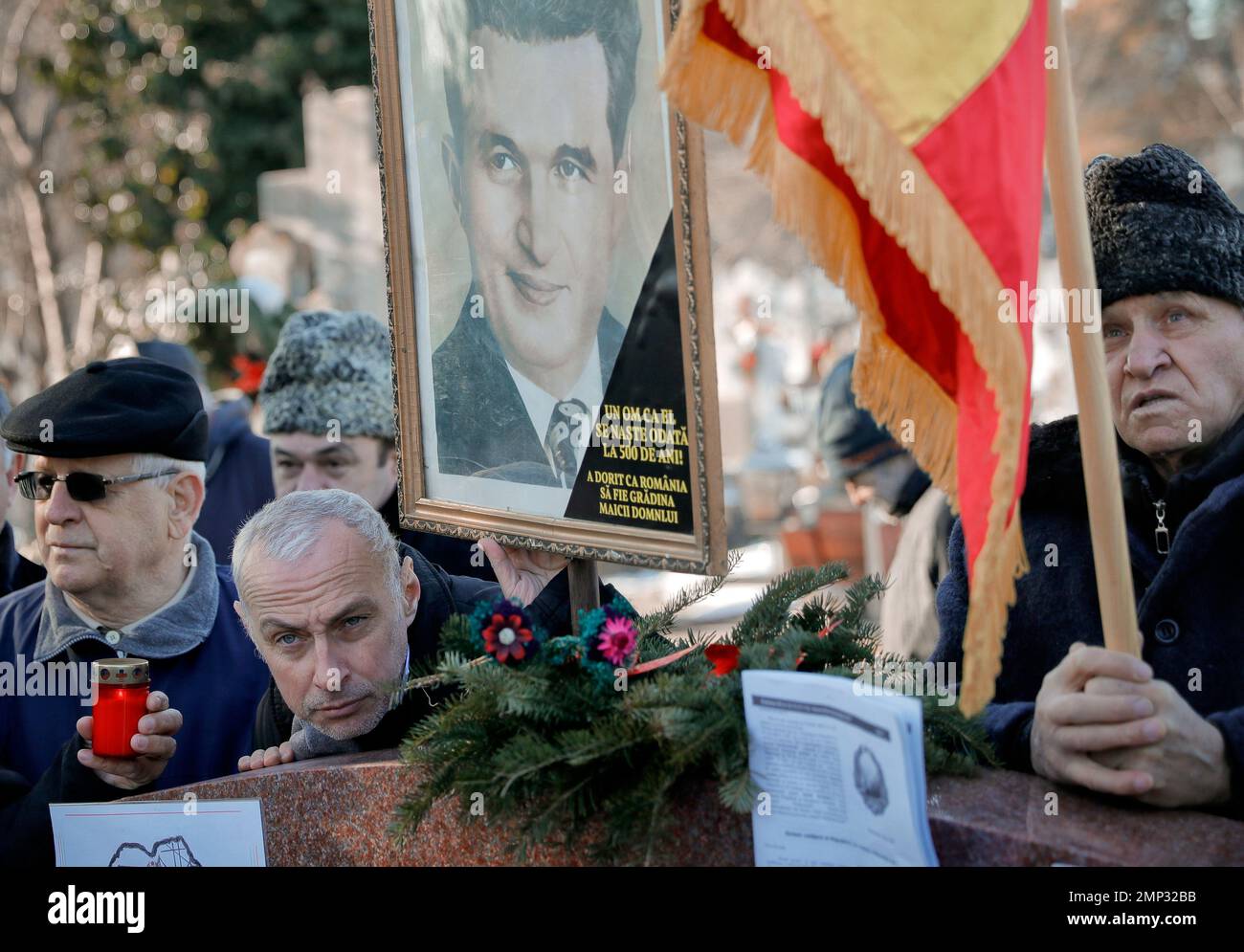 A man stands next to the official portrait of Romanian communist ...