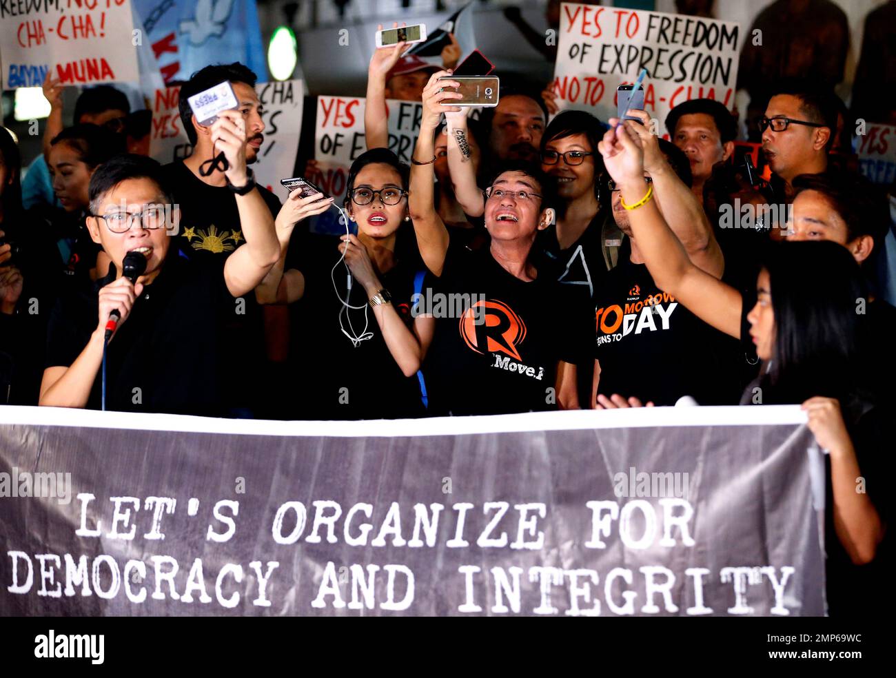 Journalists and supporters, wearing black, raise their mobile phones to ...