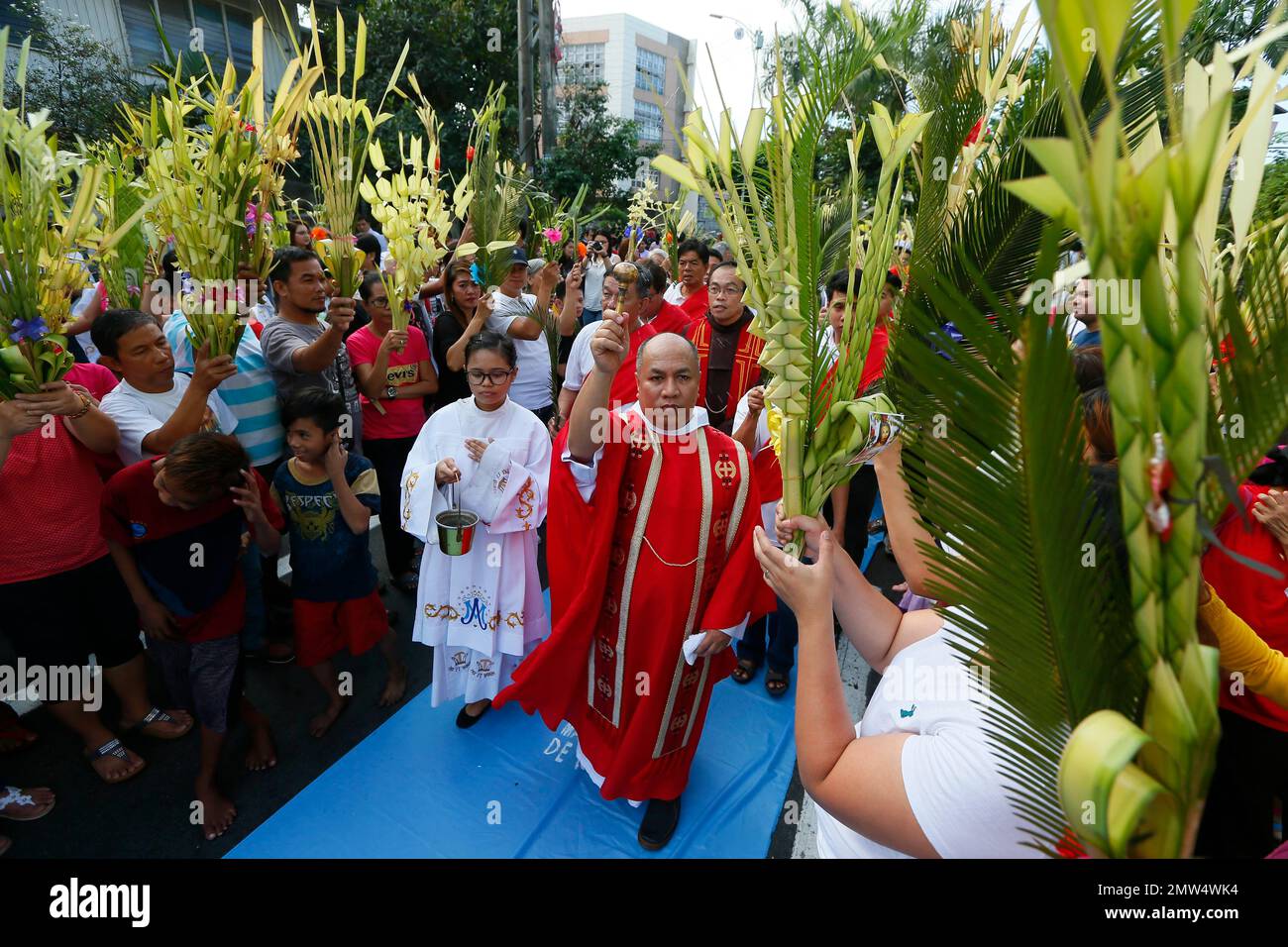 A Roman Catholic priest blesses with holy water devotees waving palm ...