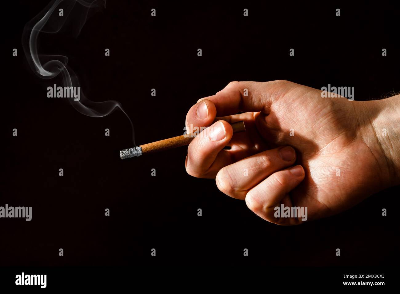 La main d'un homme tient une cigarette allumée sur un fond sombre ...