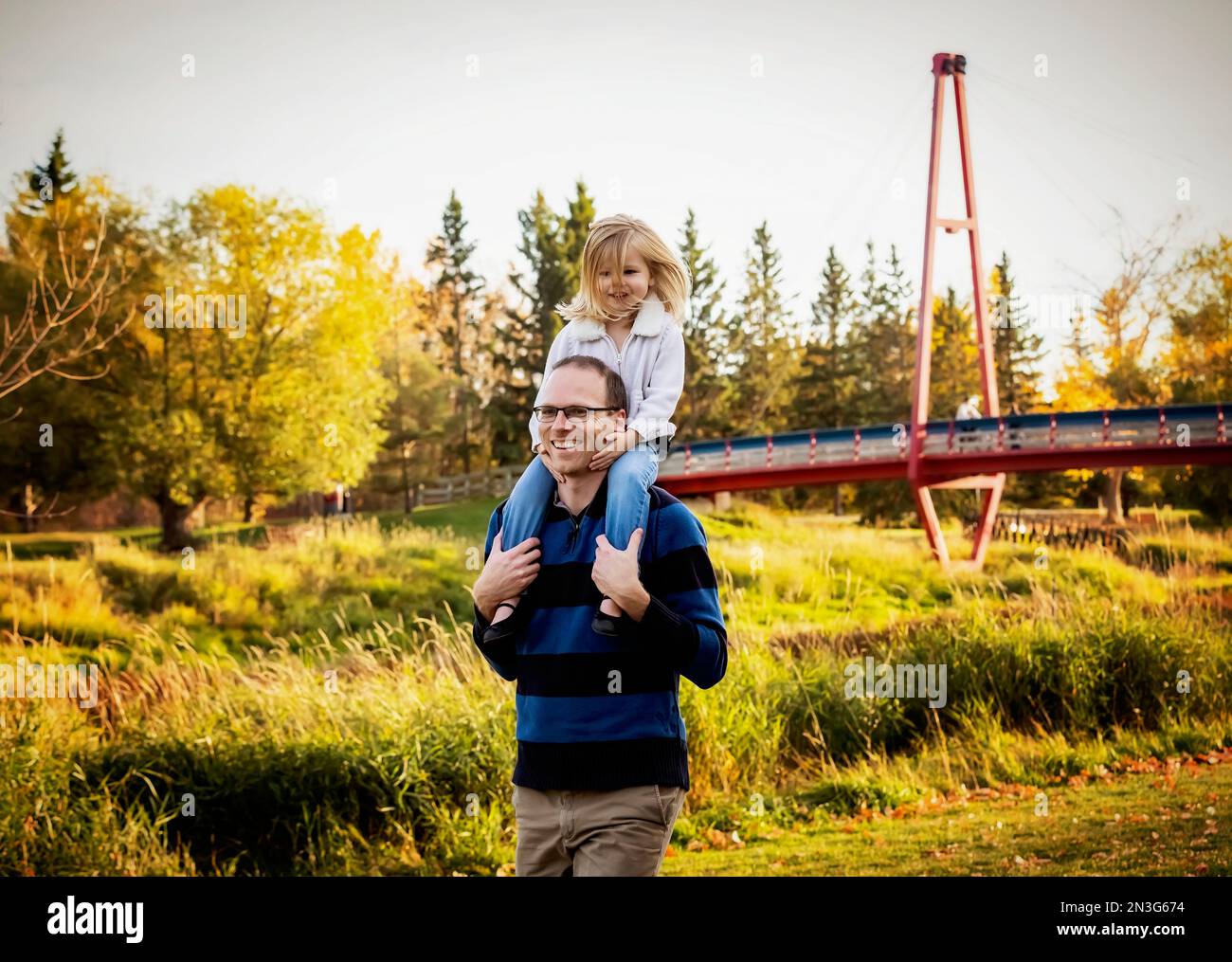 Un père portant sa jeune fille sur ses épaules tout en marchant dans un parc de la ville pendant ...