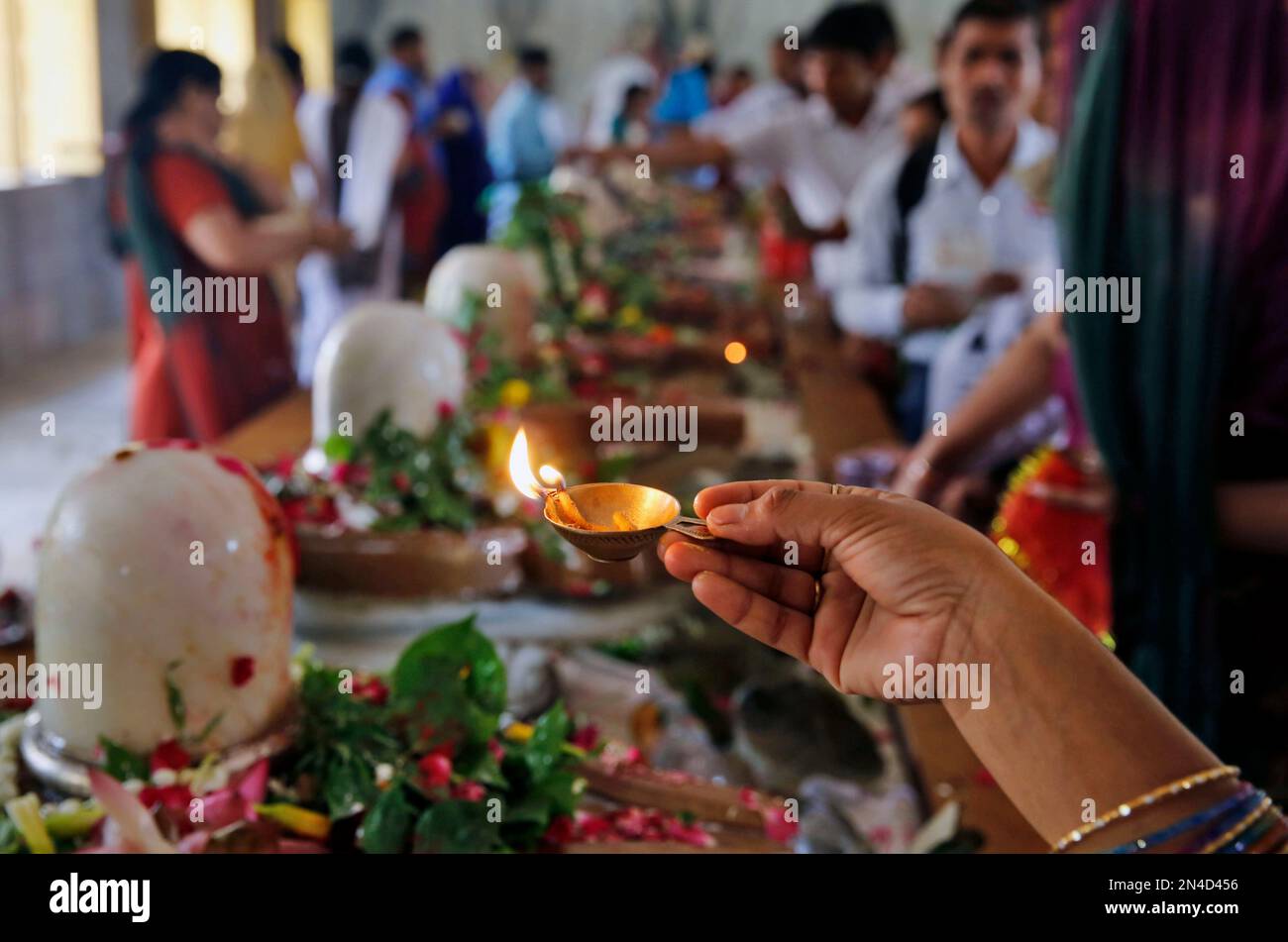 A Hindu devotee rotates an oil lamp as she offers prayers to a row of ...