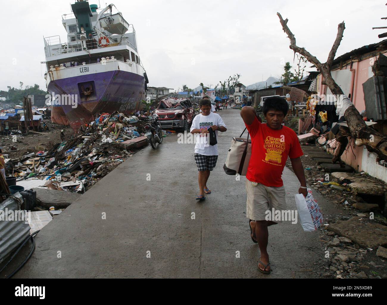 Typhoon survivors walk near shipping vessels that remain grounded after ...
