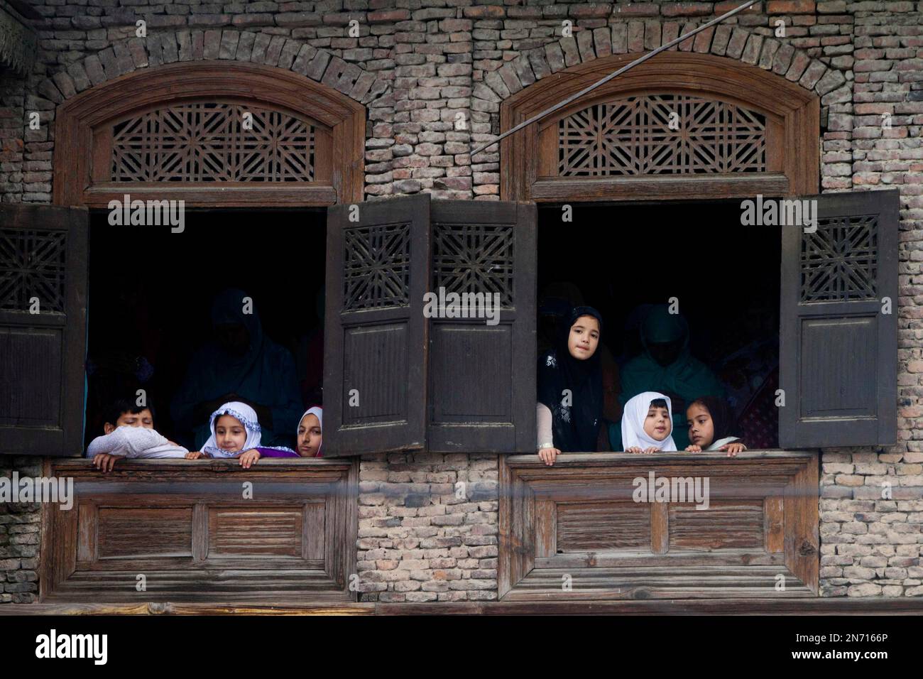 Kashmiri Muslim children watch from the window of a residential house ...