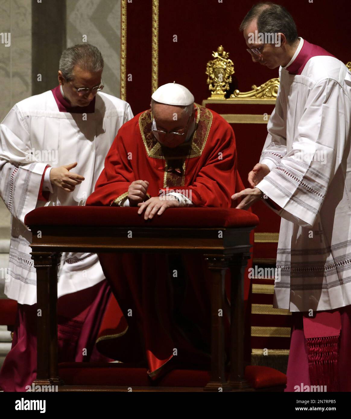 Pope Francis kneels in prayer as he is flanked by his aides, including ...