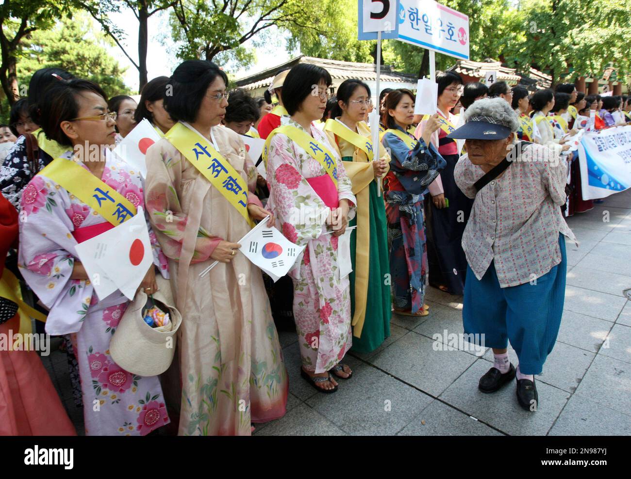 An elderly South Korean woman walks by a group of Japanese members of ...