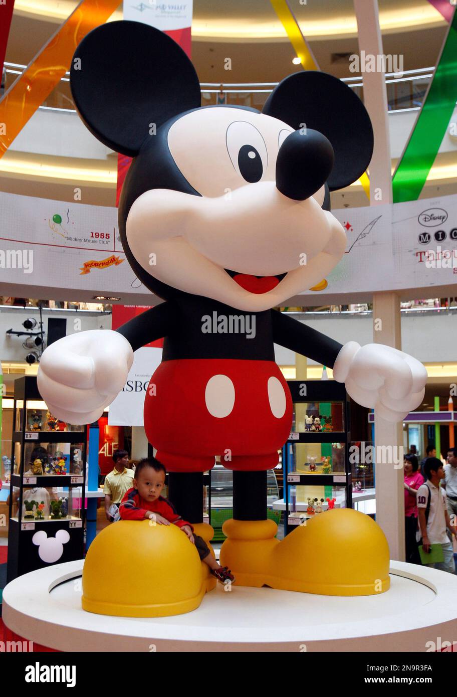 A boy sits below a giant Mickey Mouse statue on display during the ...