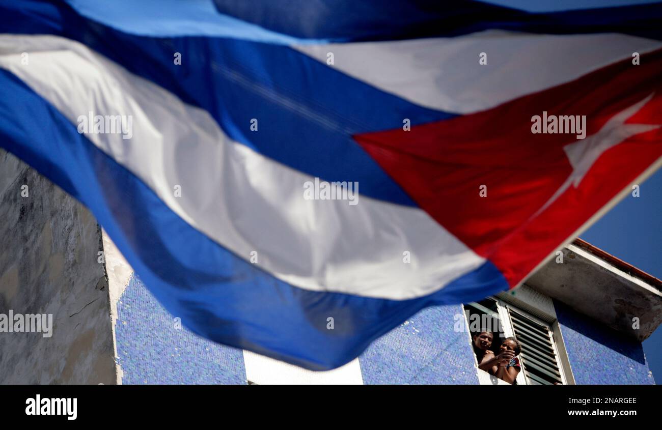 A couple look out from a balcony past Cuba's national flag at a march ...