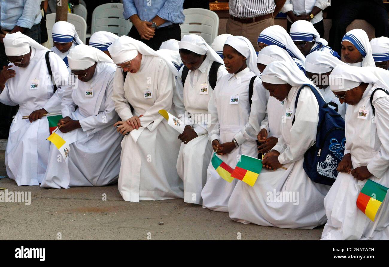 Nuns holding the Vatican and Benin's national flags kneel as they wait ...