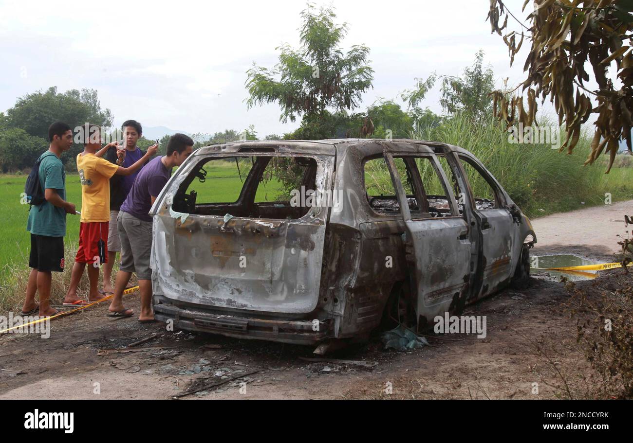 Residents look at the burnt remains of an SUV allegedly owned by slain ...