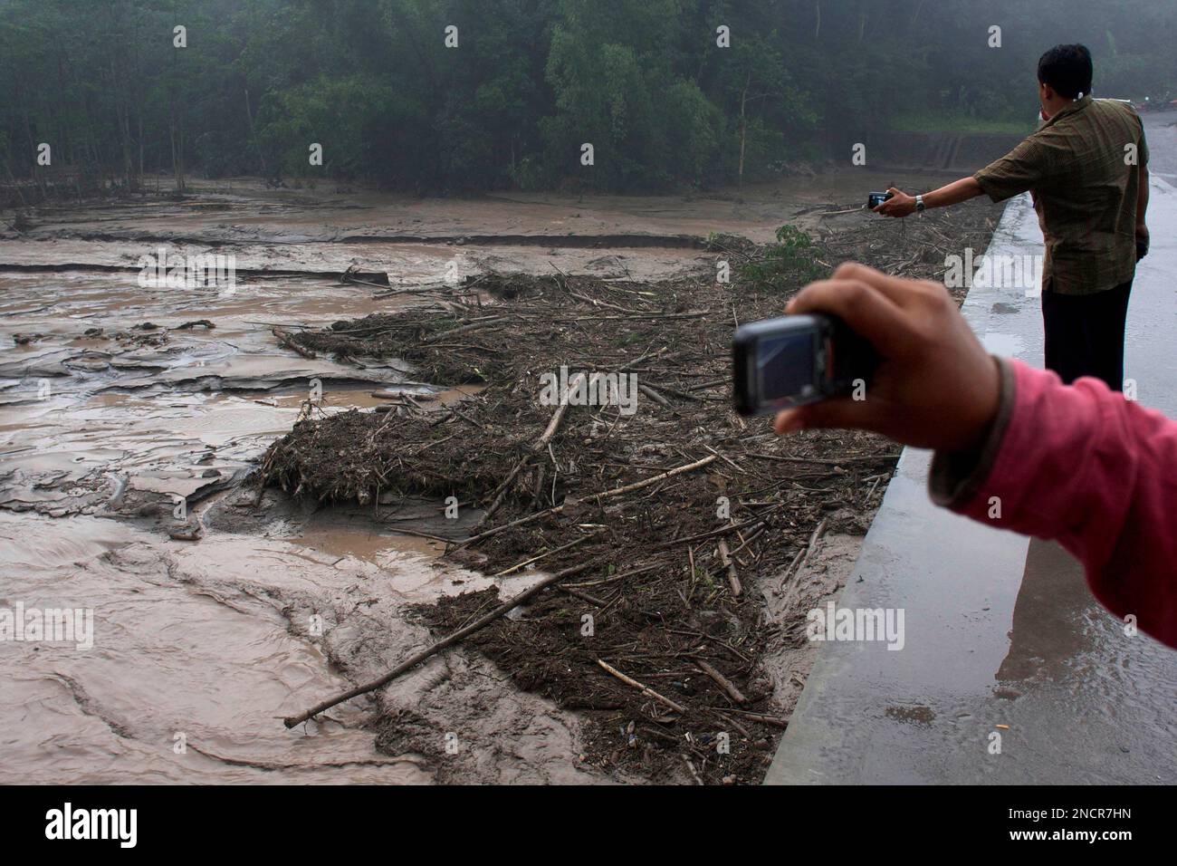 Indonesian men take pictures of logs and volcanic materials carried by ...