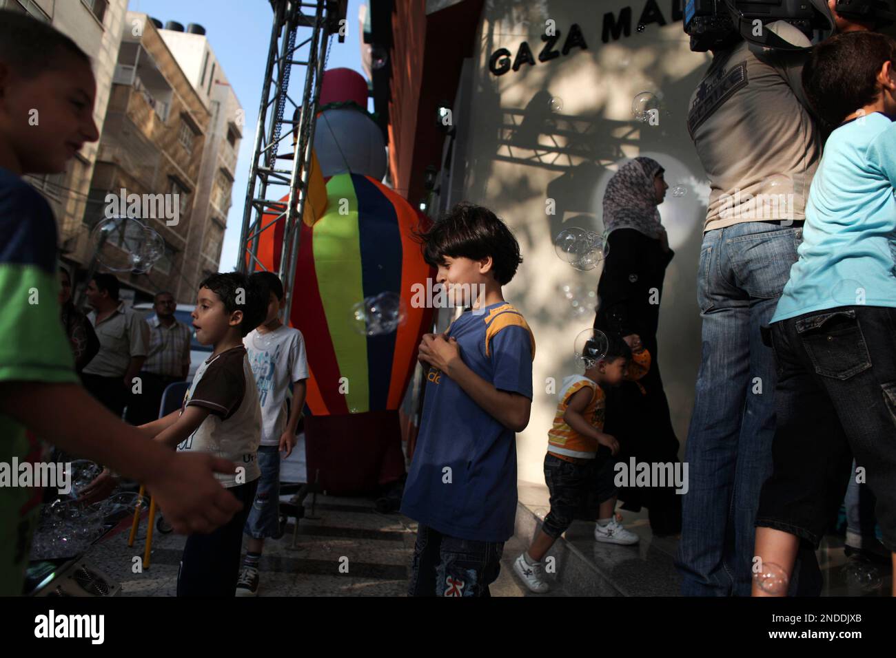 Palestinian children play with bubbles as people walk into the newly ...