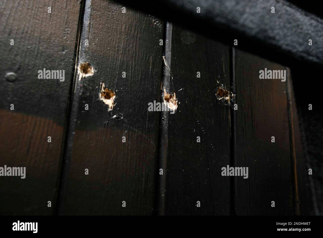Four bullet holes are visible in the wood panel behind the chair in the ...