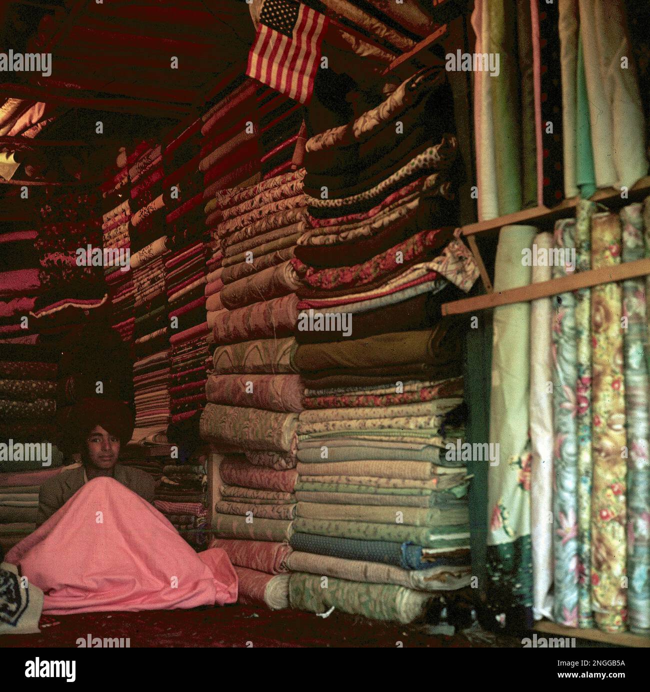 A shopkeeper is shown in a cloth shop where a small American flag is ...