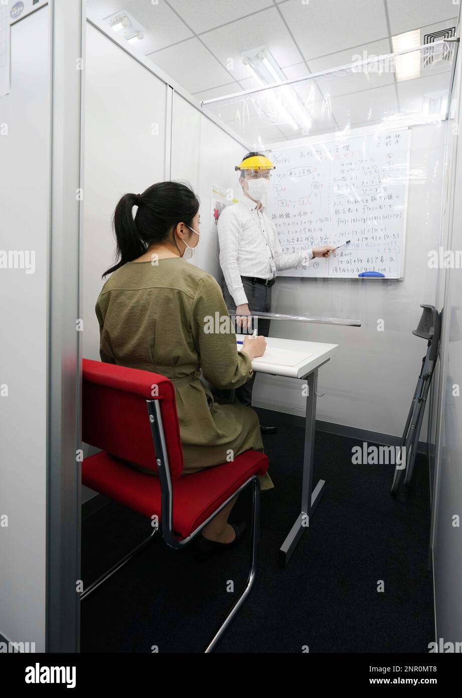 A teacher wearing a face shield teaches through a vinyl sheet at a ...