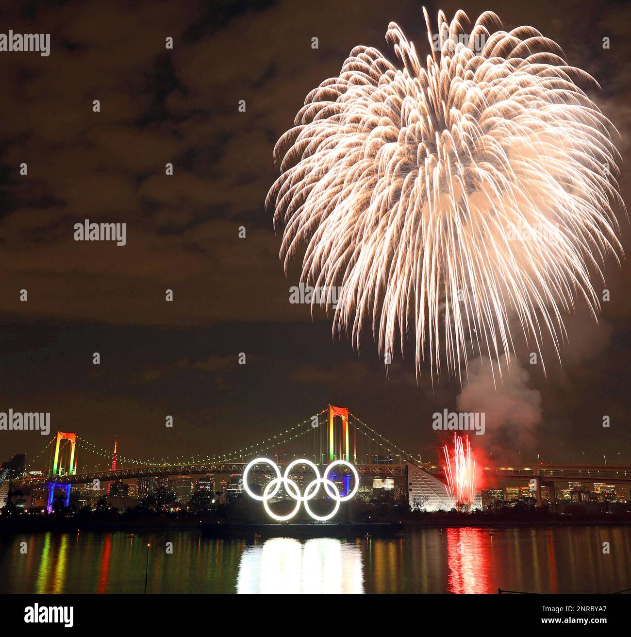 A monument of five-ring emblem is lit up on the water with fireworks to ...