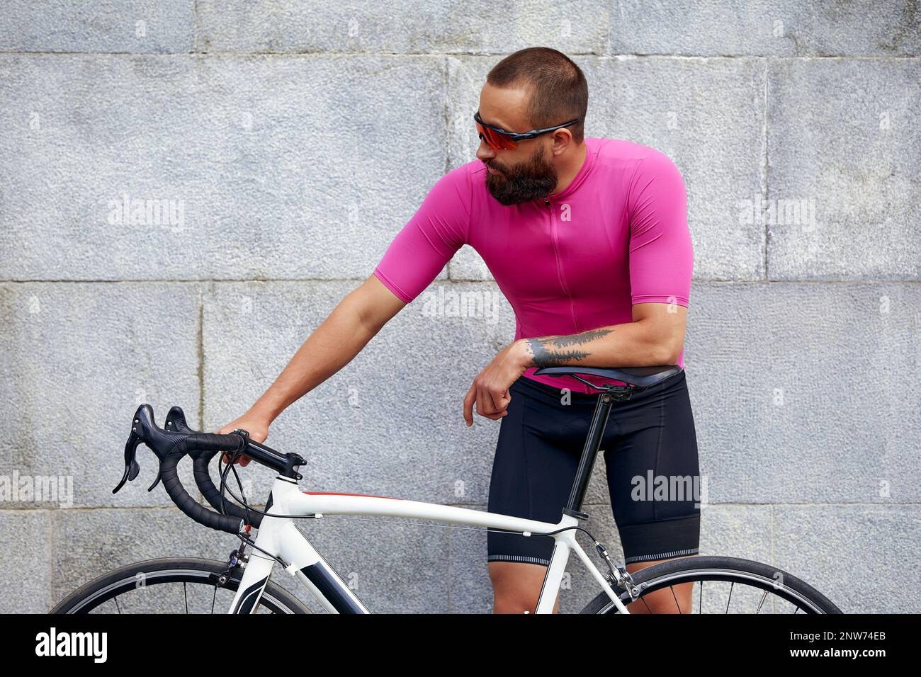 Un cycliste barbu en lunettes avec un vélo sur le fond d'un mur gris ...