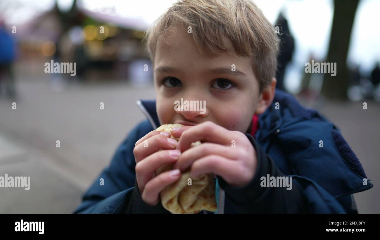 Petit garçon mangeant des crêpes dehors dans la rue de ville pendant la ...