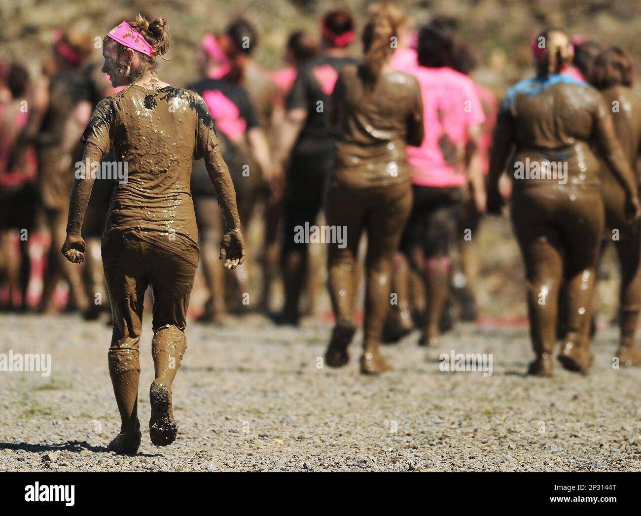 A participant is covered from head to toe in mud as she walks with her ...