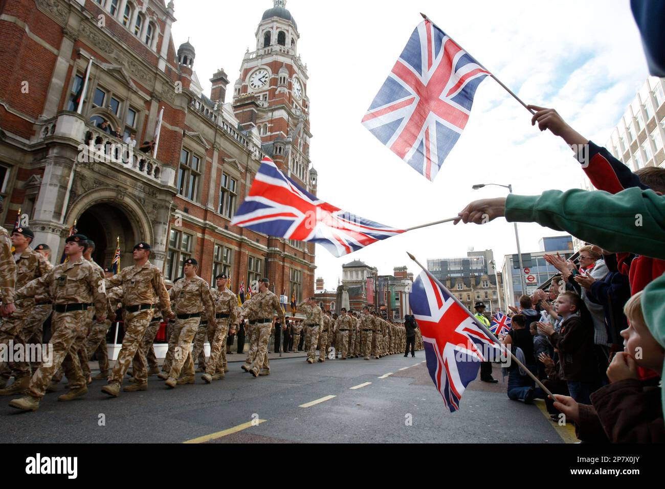 People line a street outside the town hall wave their flags as soldiers ...