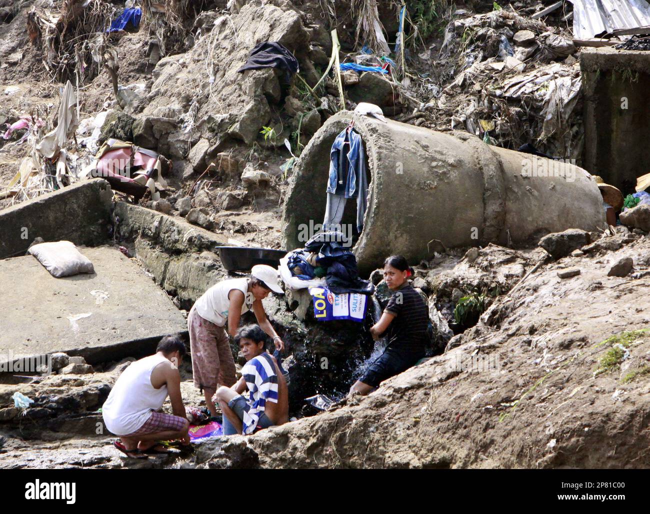 People use a broken sewer line to wash their muddied clothes after ...