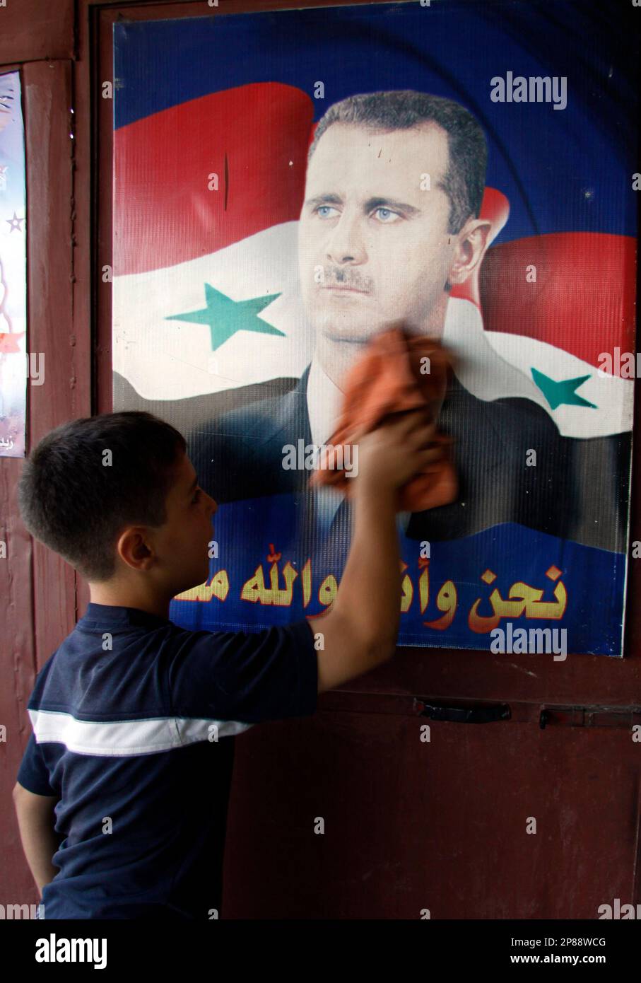 A Syrian boy cleans a poster of Syrian President Bashar Assad reading ...