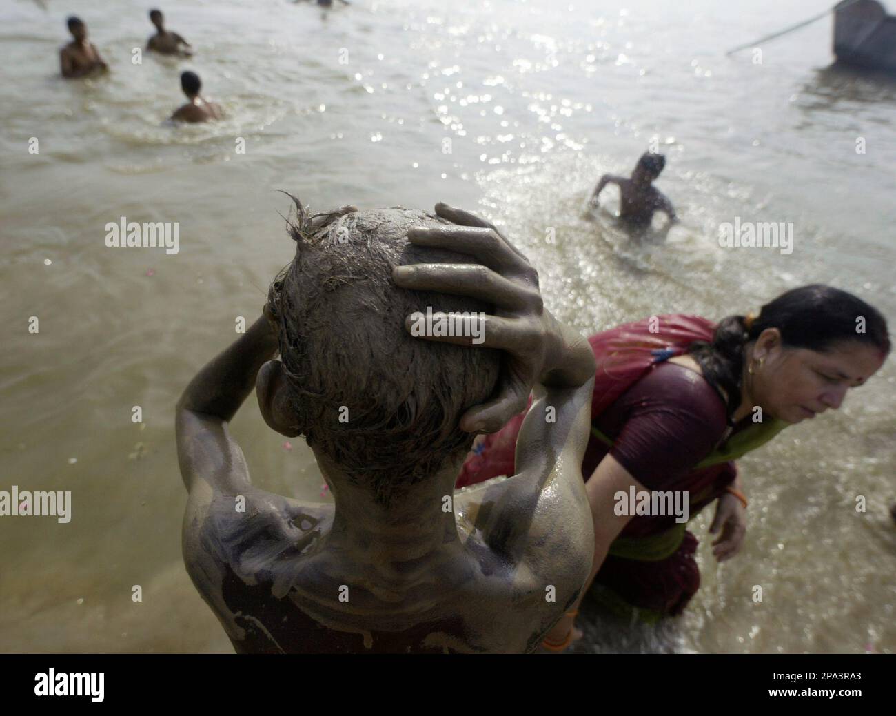 A child smears his body with mud before taking a holy dip in river ...