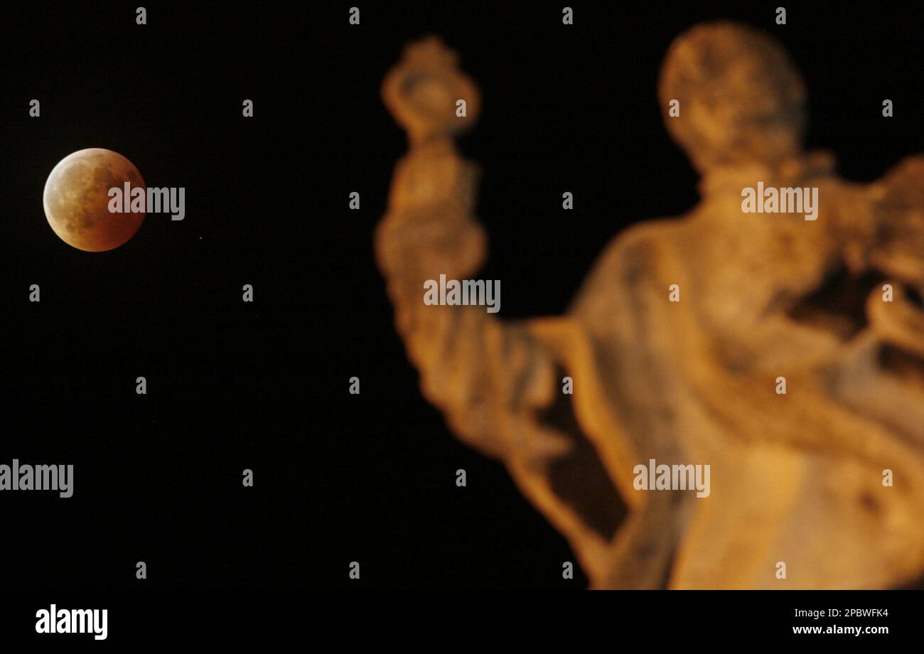 The moon is seen over one of the statues that top the colomnade of St ...