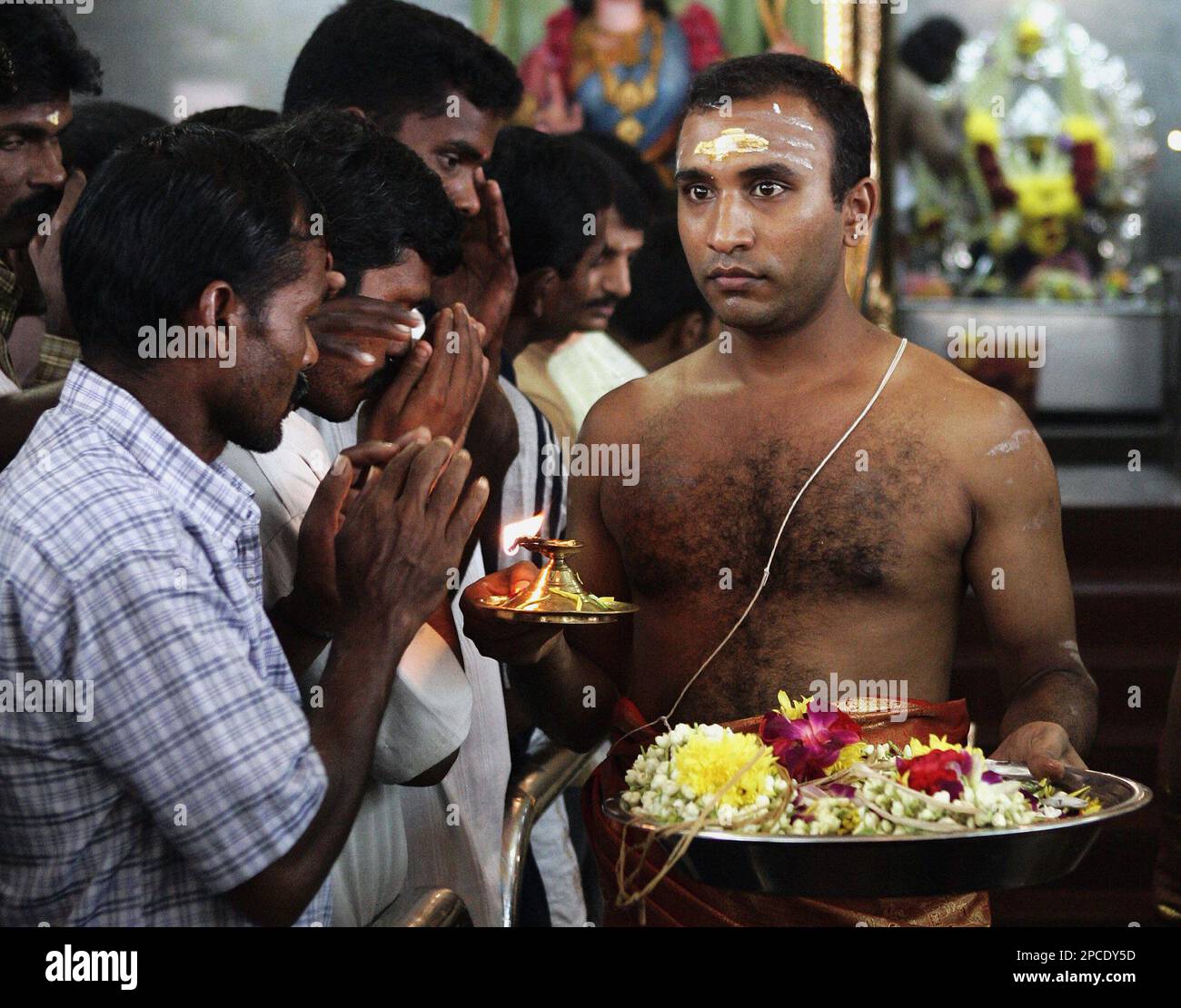 Hindu devotees offer prayers as a priest gives out flowers to devotees ...