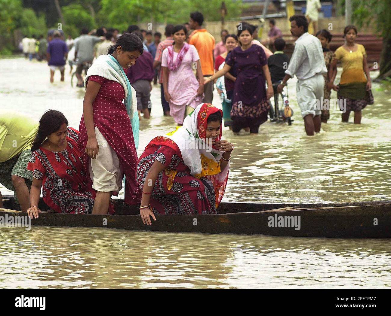 Women try to settle on a country boat as others wade through a flooded ...