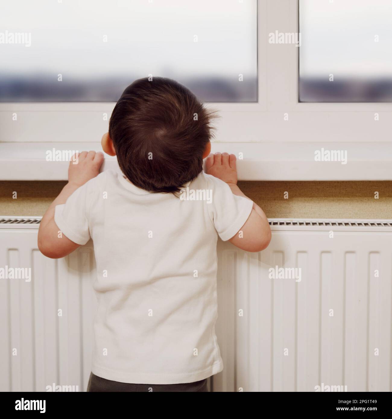 Bébé monte à la fenêtre près de la batterie chauffante. Un petit enfant ...