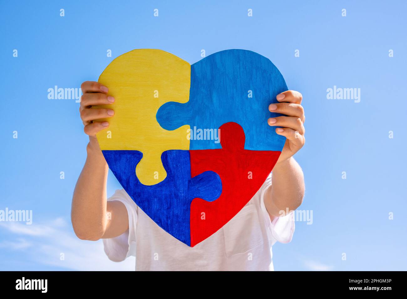 Mains de garçon tenant le coeur de puzzle coloré sur fond bleu ciel ...