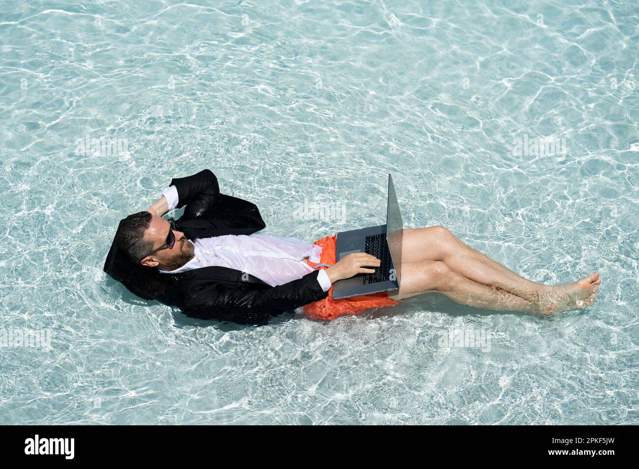 Drôle d'homme d'affaires en costume travaillant avec un ordinateur sur la plage de mer. Concept ...