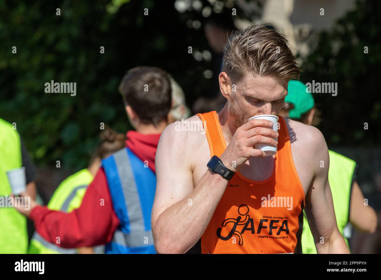 Le coureur d'une course sur route de 10km boit de l'eau dans une tasse ...