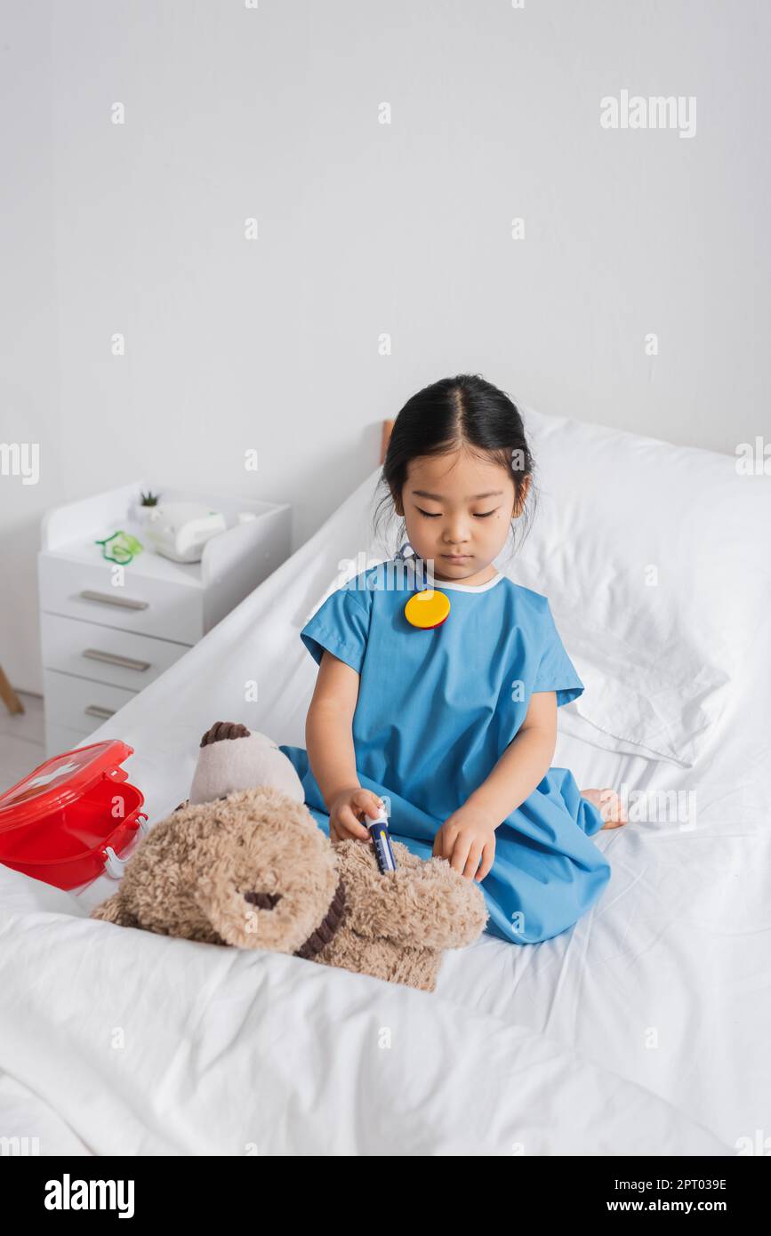 enfant asiatique dans la robe d'hôpital faisant l'injection à l'ours en ...