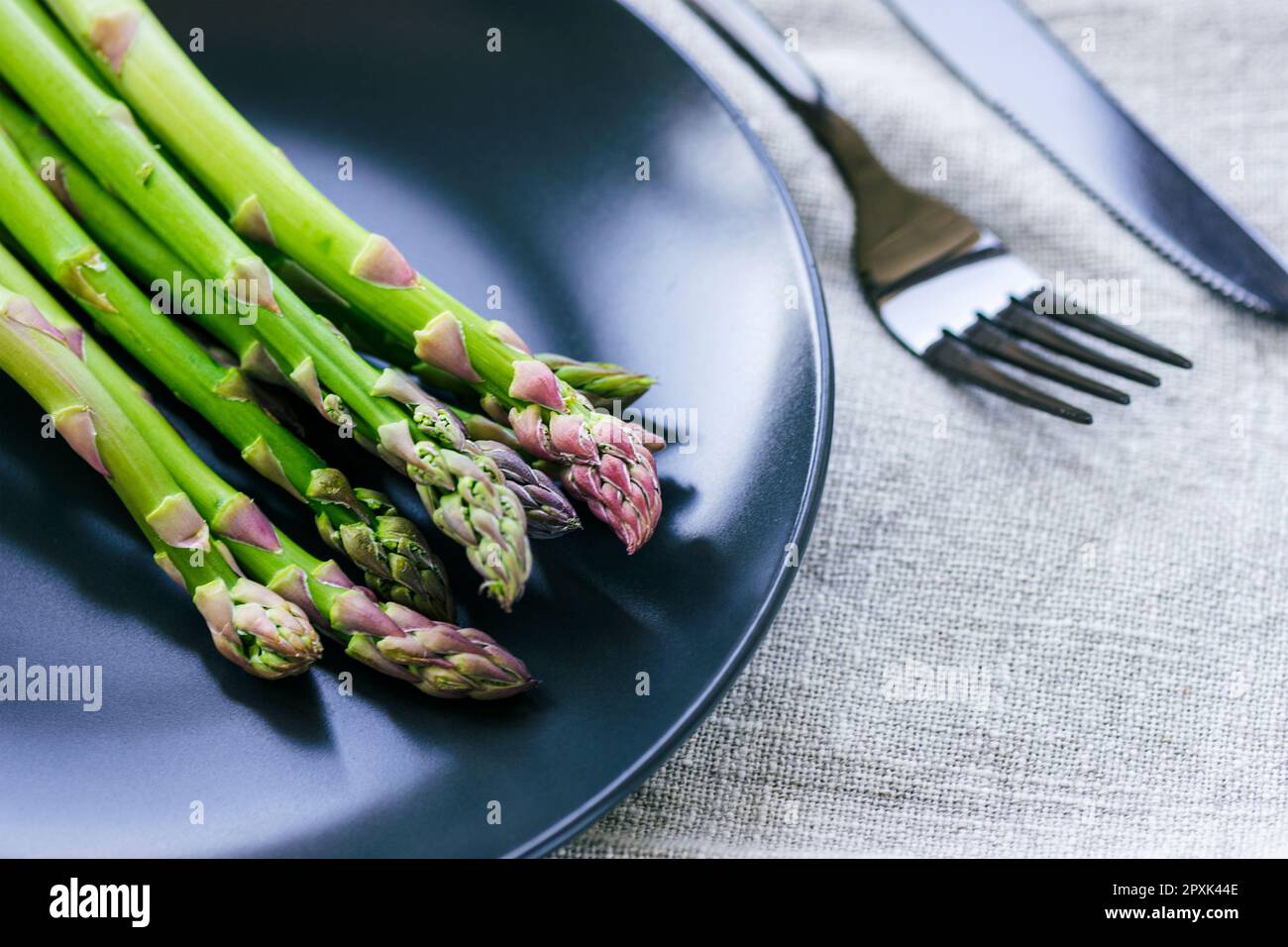 Asperges vertes fraîches sur une assiette noire sur une serviette en ...
