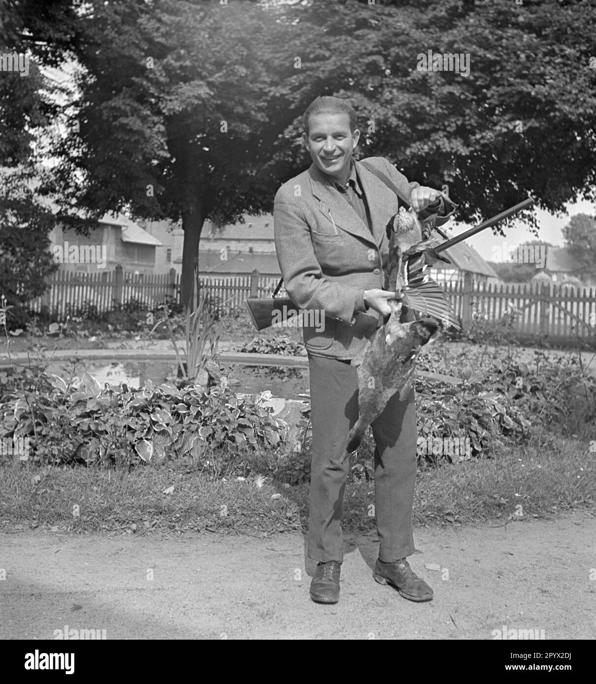 Un homme bien habillé posant avec un canard en feu devant un étang. C ...