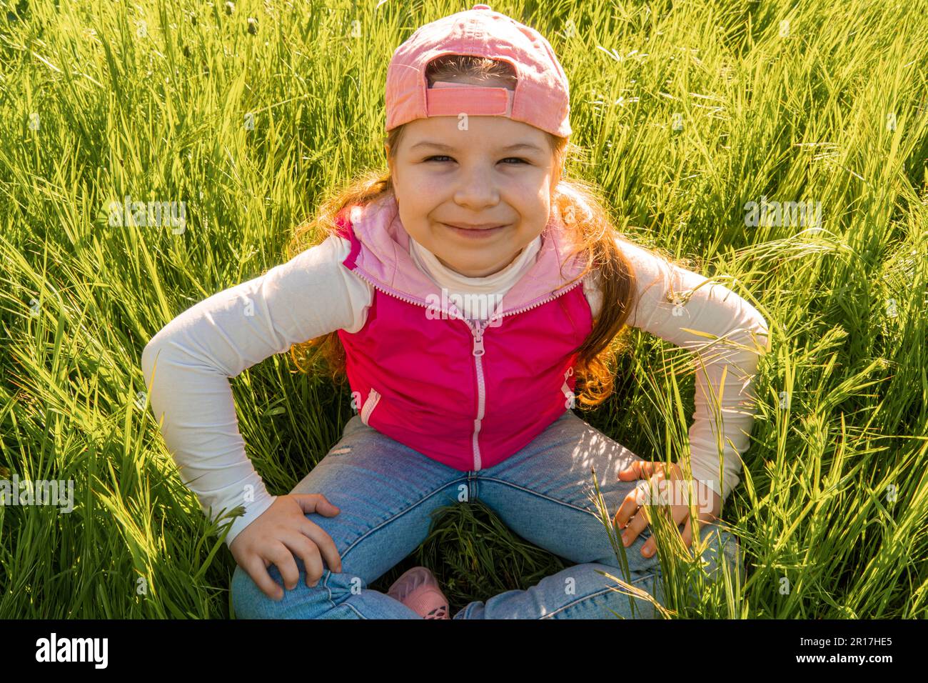 Une jeune fille gaie est assise dans l'herbe verte épaisse avec ses mains sur ses genoux ...