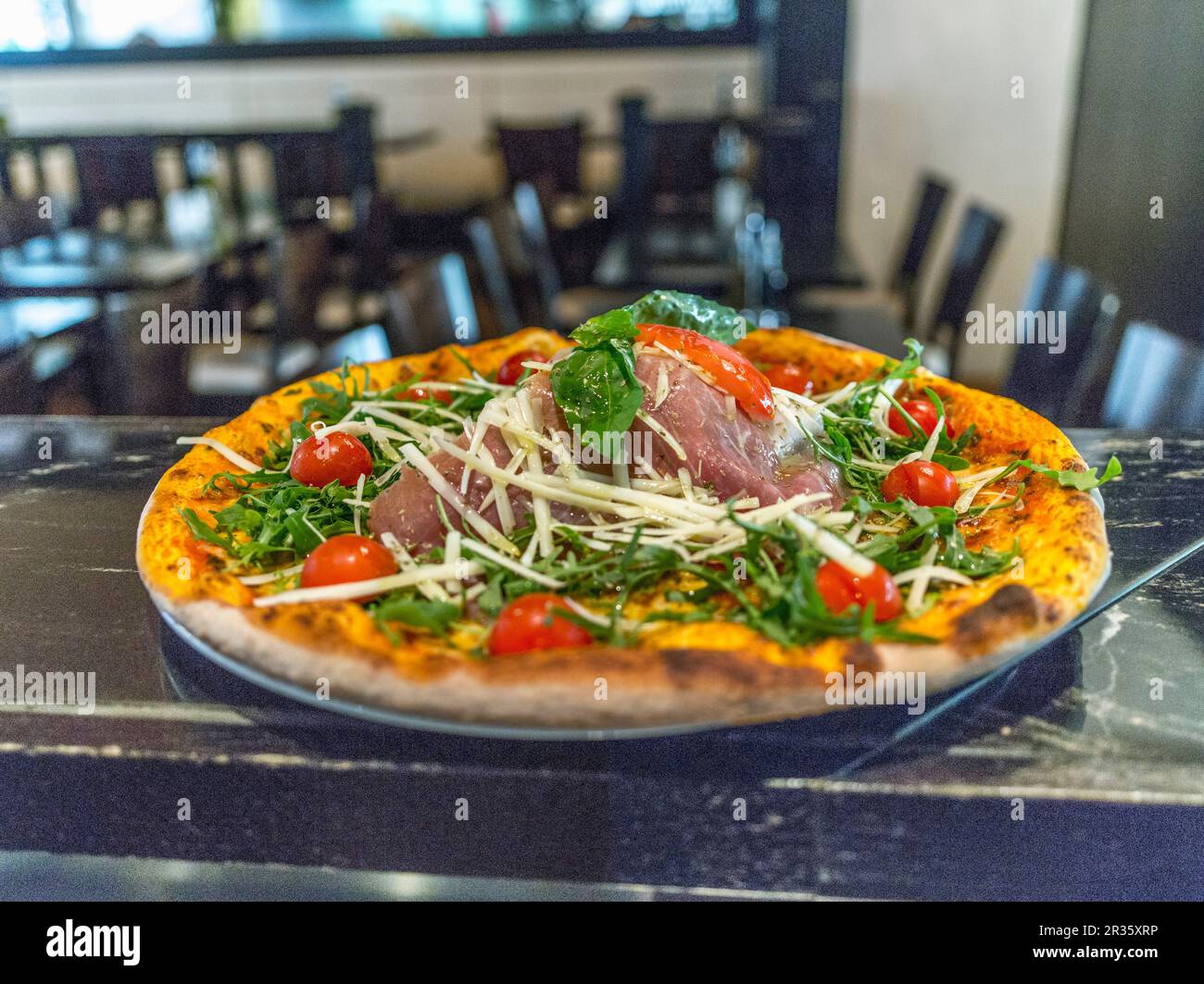 Une pizza au jambon de Parme, aux roquette et aux tomates cerises dans ...
