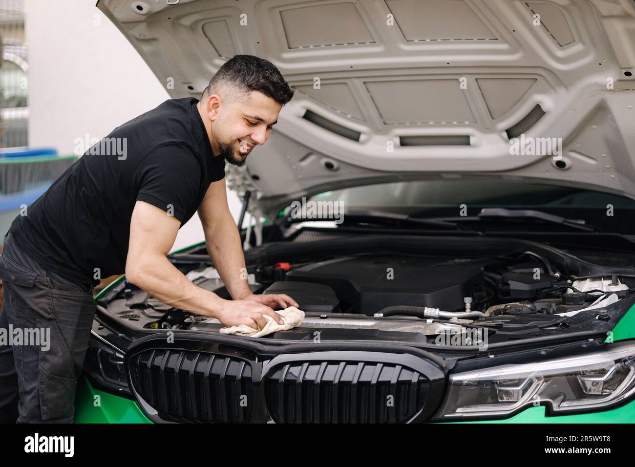 Portrait d'un mécanicien de sexe masculin travaillant dans son garage. Un jeune barbu vérifie le ...
