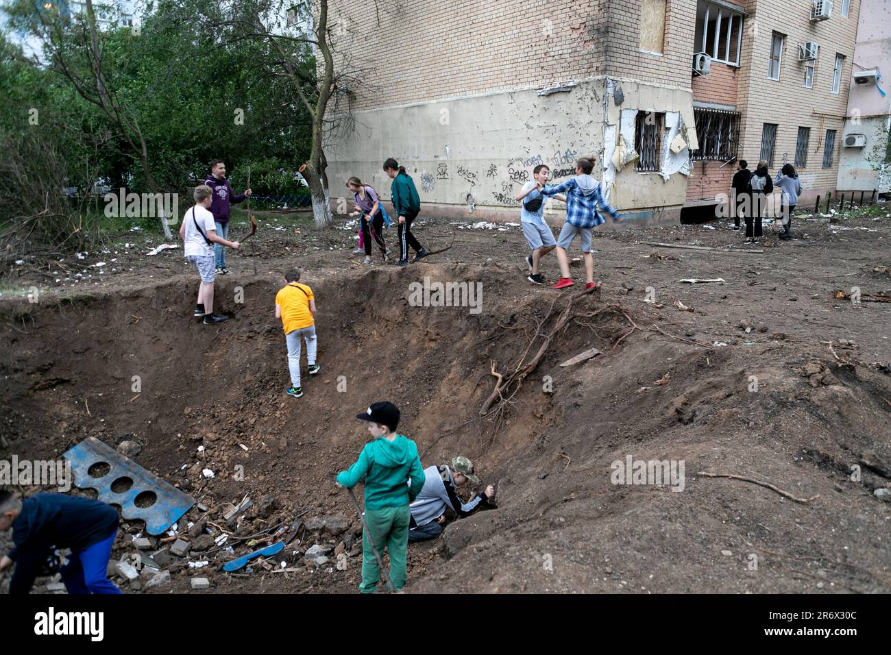 Les enfants jouent dans un cratère près du bâtiment résidentiel détruit ...